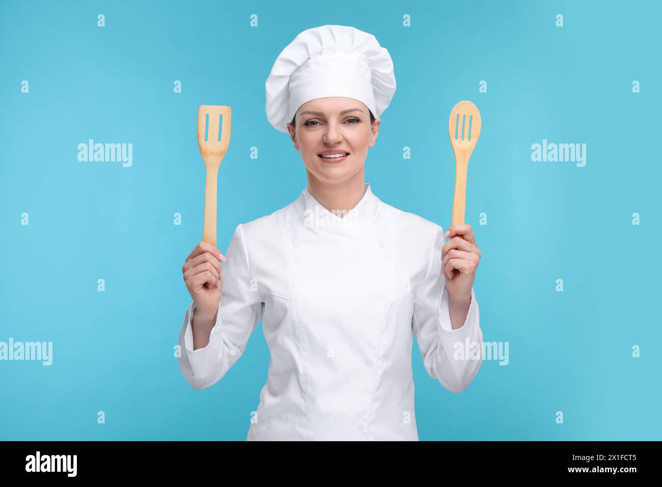 Happy chef in uniform holding wooden spatulas on light blue background ...