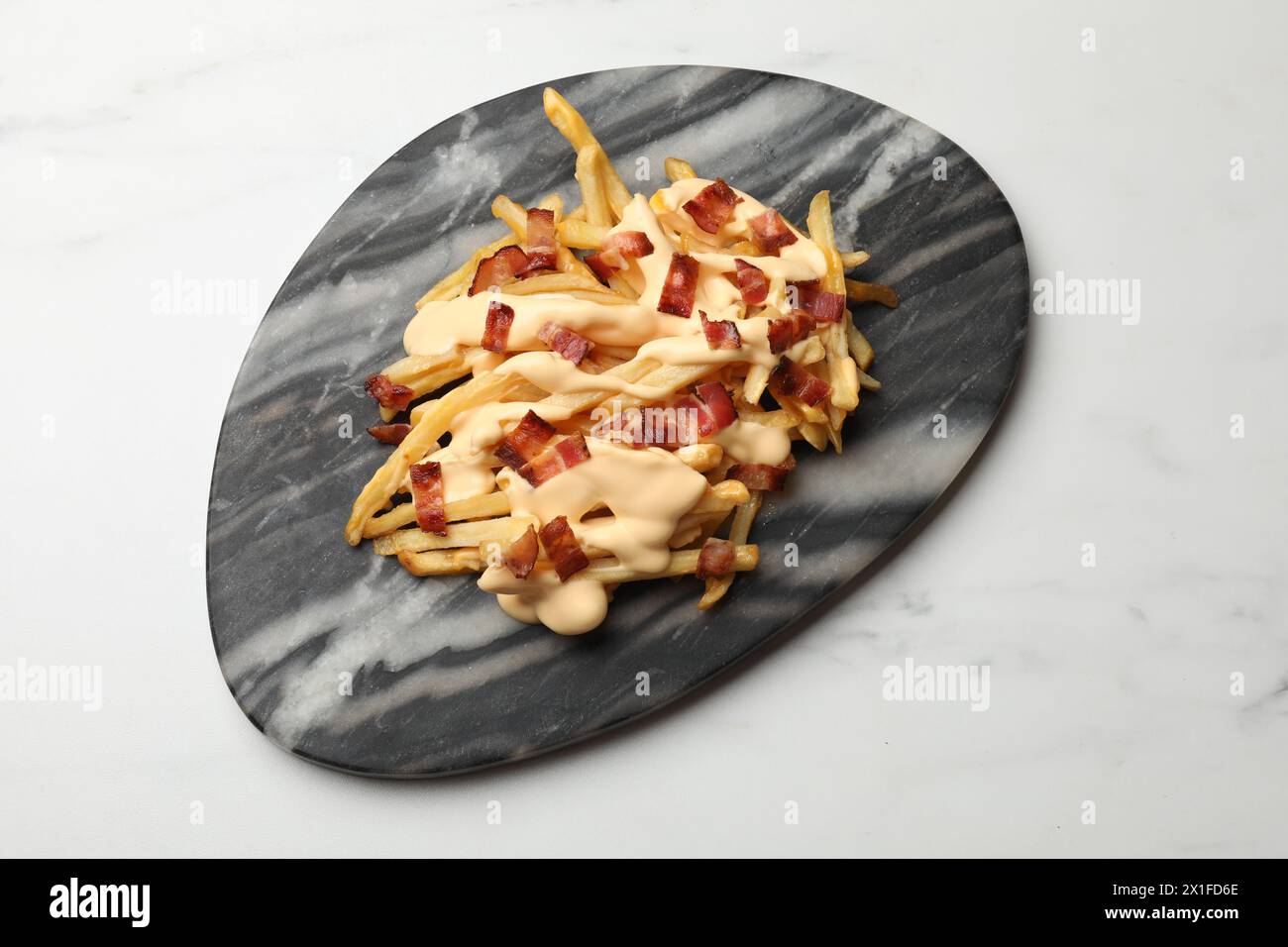 Delicious French fries with bacon and cheese sauce on white marble ...
