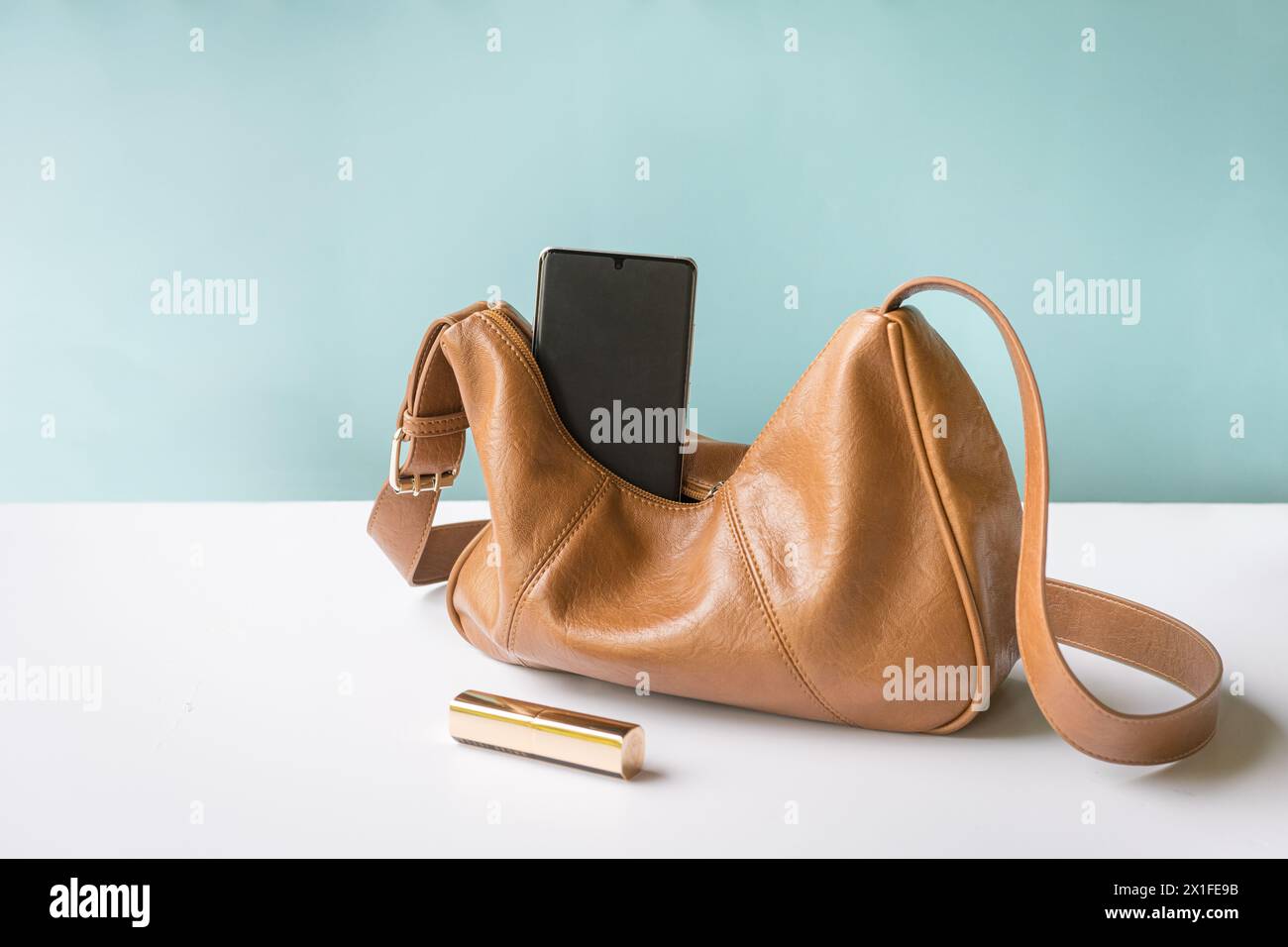Woman leather handbag with phone and lipstick. On white table and blue ...