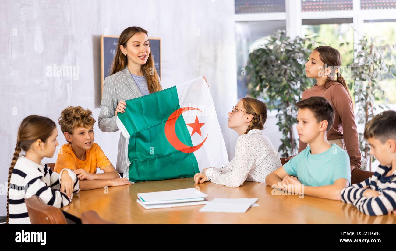 Positive young female teacher holding national flag of Algeria while ...