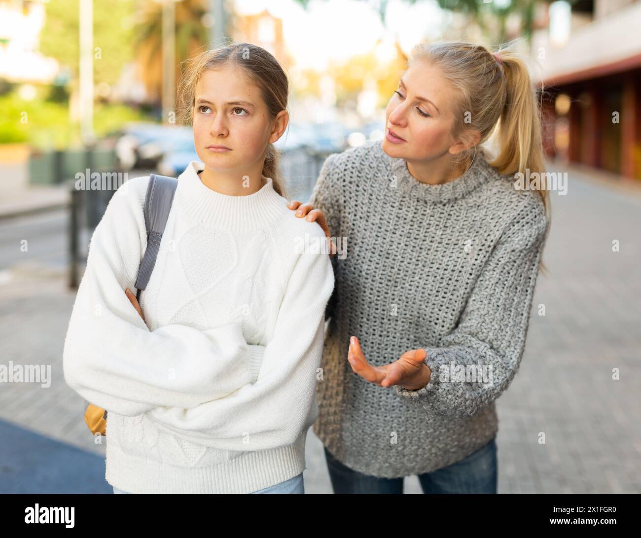 Upset teen girl walking on city street with worried mother reproaching ...