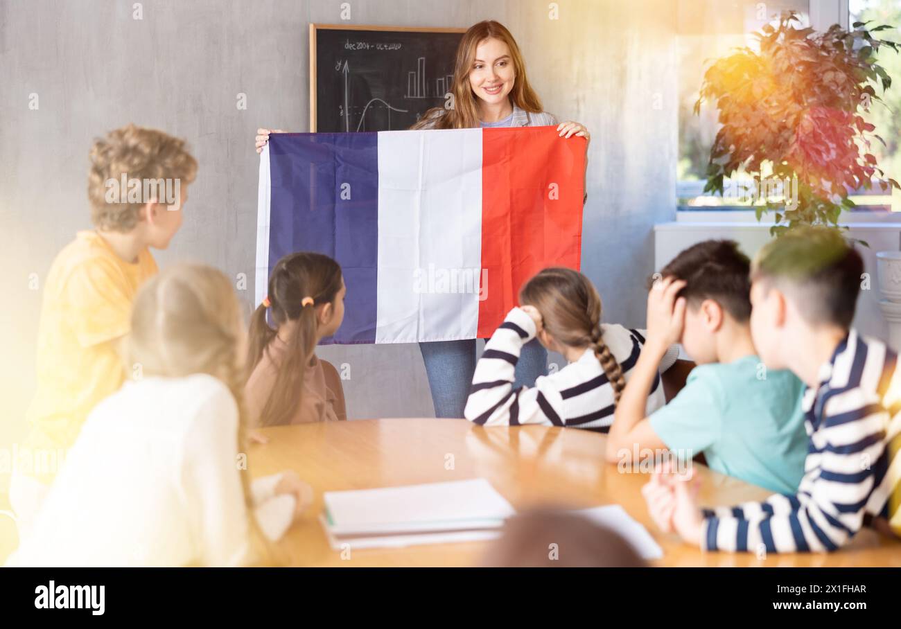 Excited young woman teacher showing national flag of France and telling ...