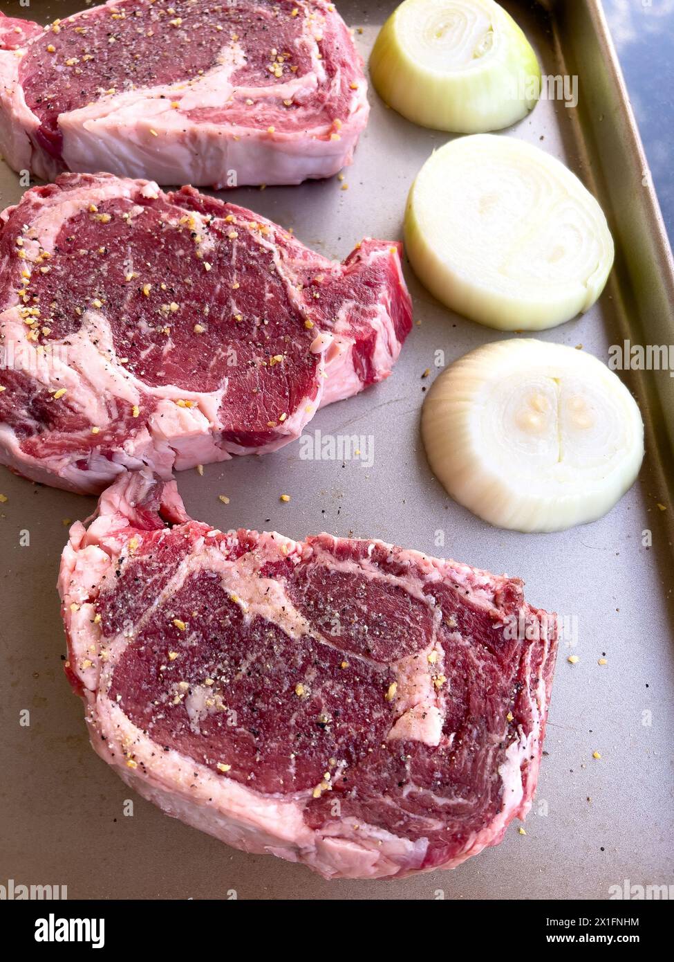 Raw Ribeye Steaks Seasoned with Spices and Onion Halves on Tray Stock ...