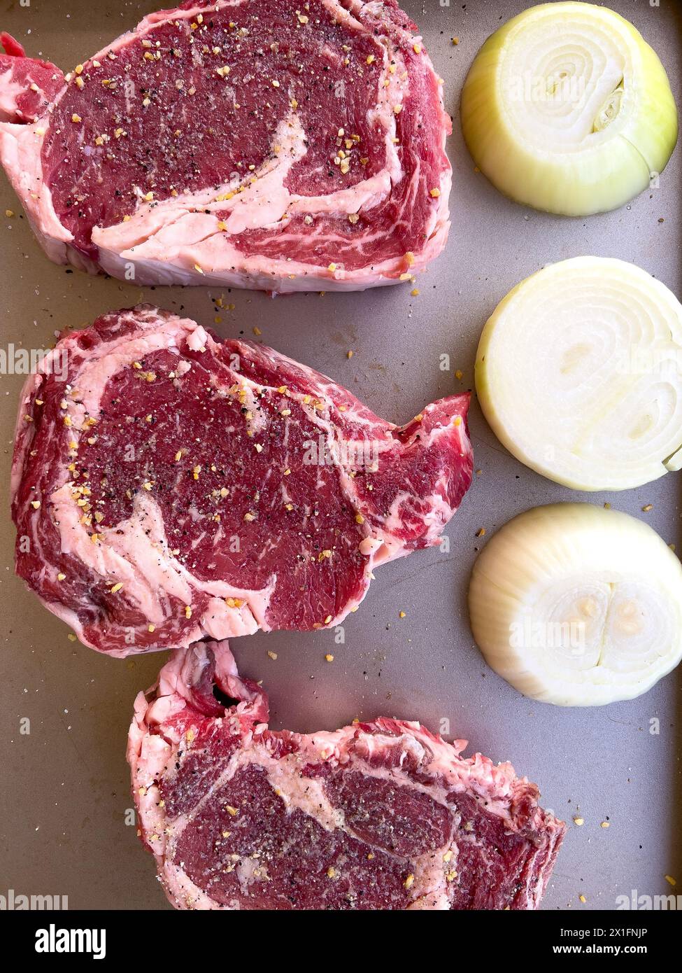 Raw Ribeye Steaks Seasoned with Spices and Onion Halves on Tray Stock ...