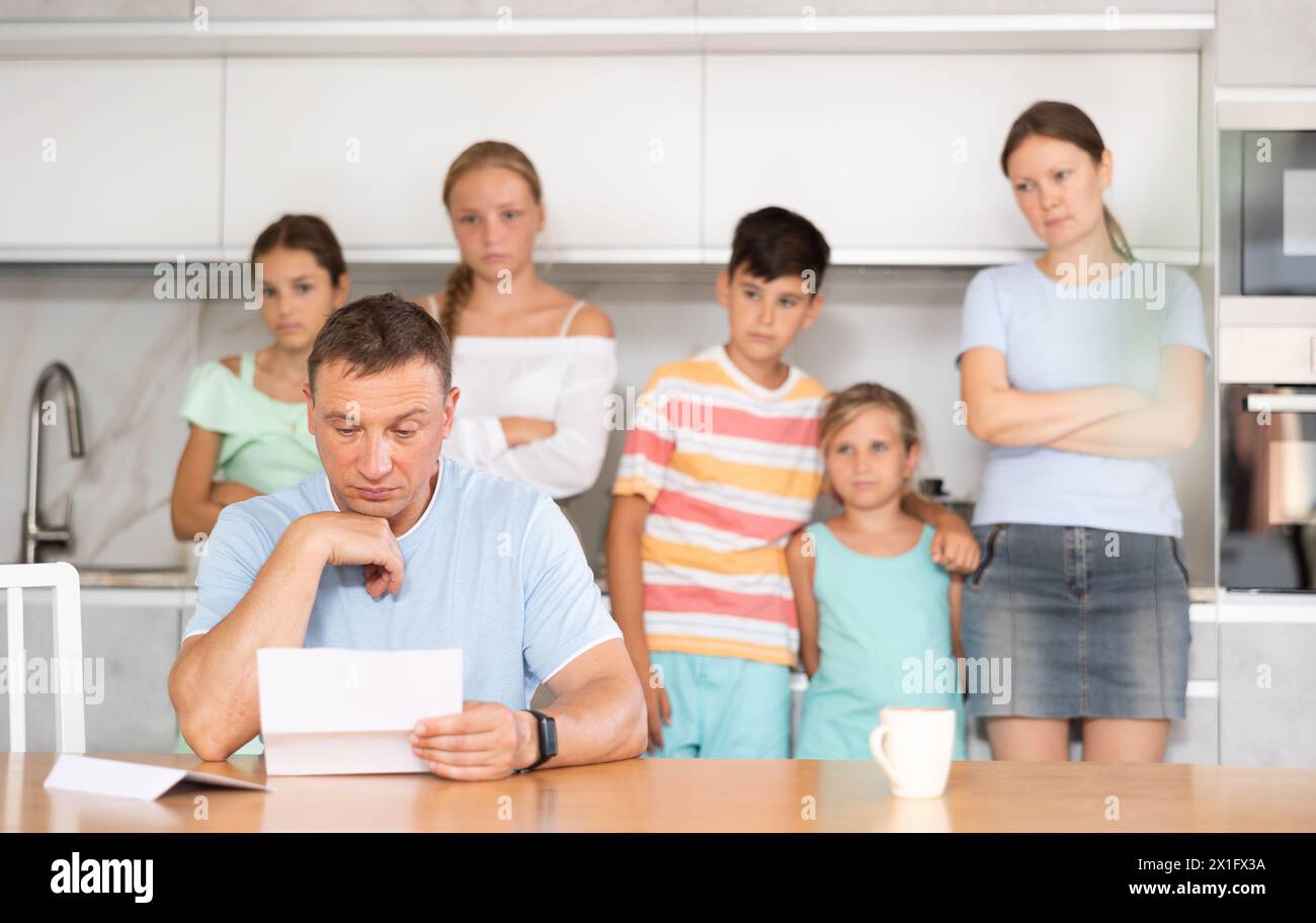 Frustrated dad is sitting in kitchen, reading letter. Blurred worried ...
