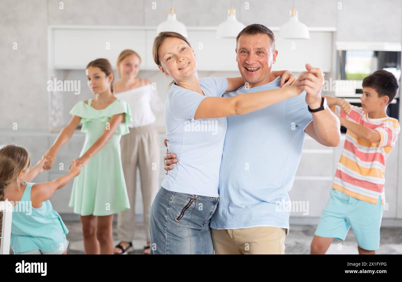 Happy cheerful parents together with children dancing in living room at ...