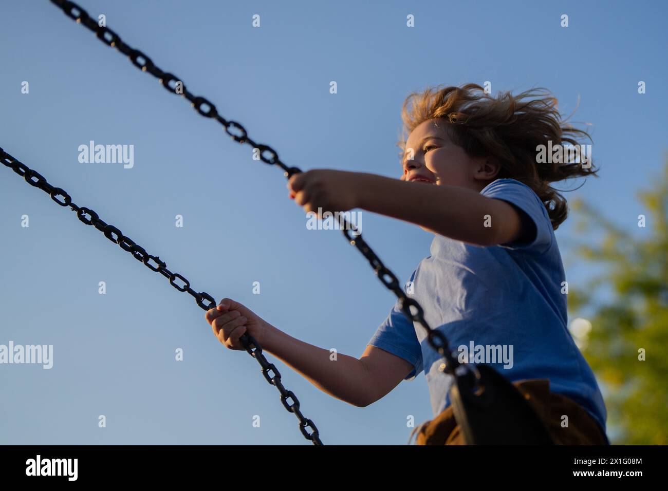 Kid swinging high. Adorable blonde child having fun on a swing on ...