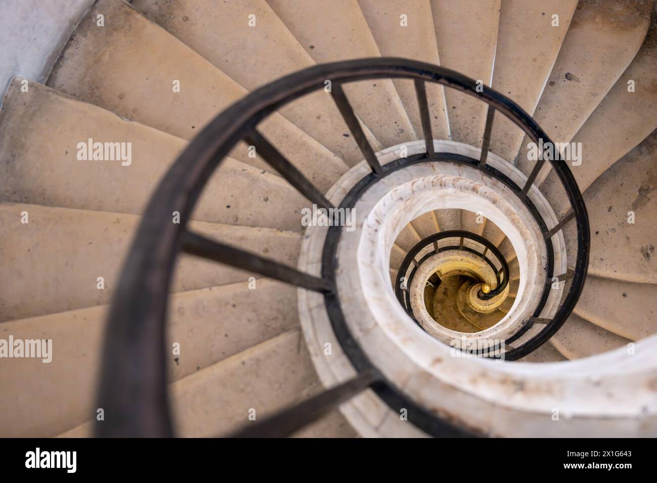 A top-down view of a spiral staircase creating an optical illusion with its descending coils ...