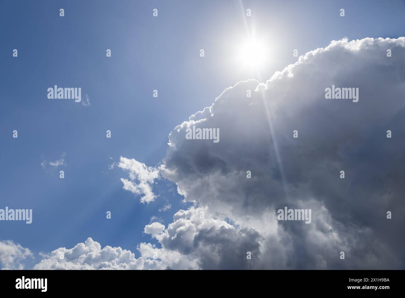 Sunlight piercing through billowing cumulus clouds against a vivid blue ...