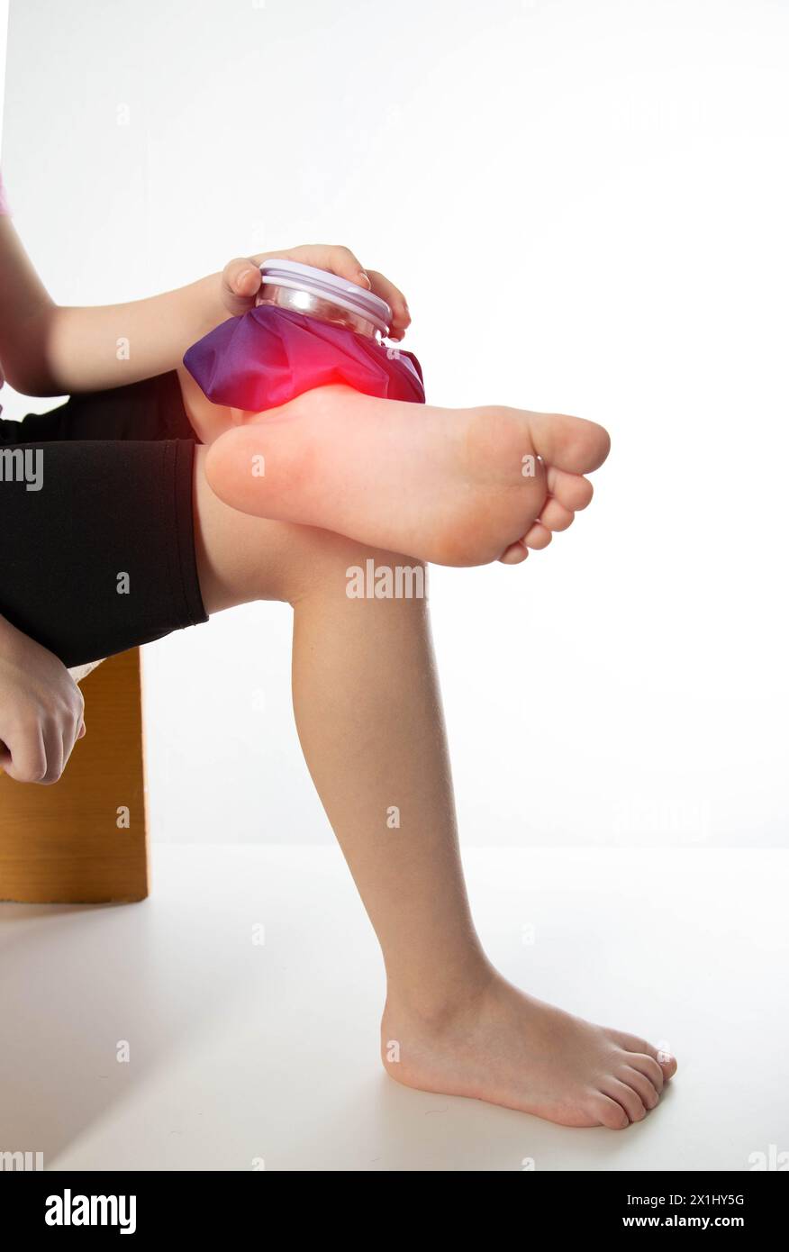 A girl applies a blue medical bag with ice to her ankle joint for a ...