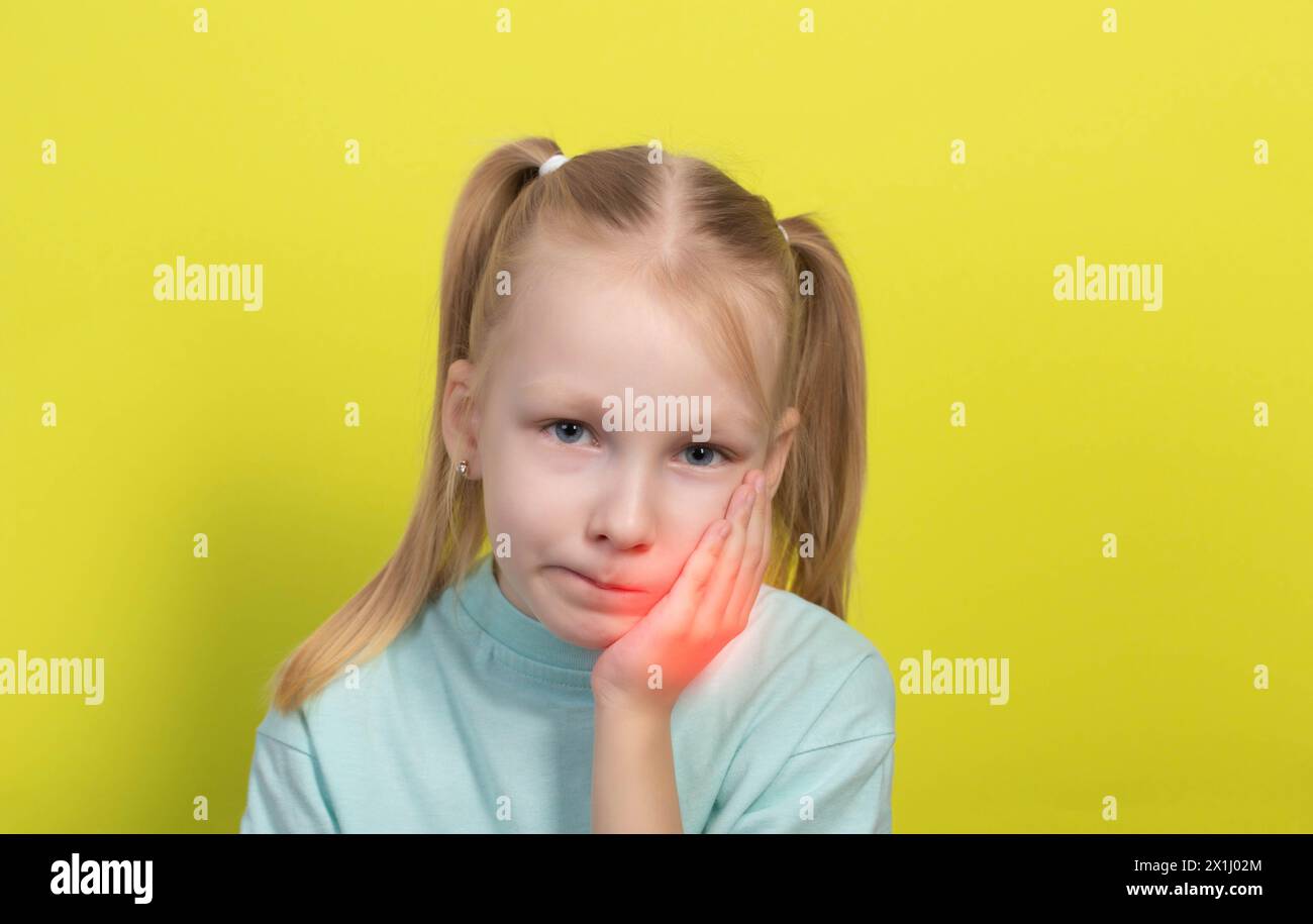 A little girl aged seven years old holds her cheek with her hands on a ...