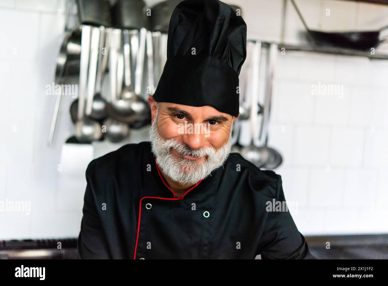 Cheerful male chef with a beard in a black uniform smiles in a ...