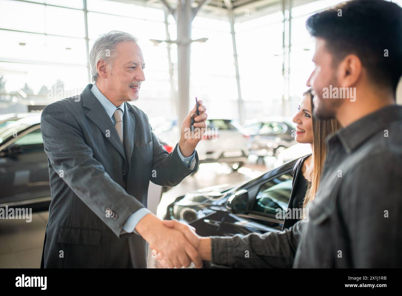 Car dealer giving an handshake and giving keys to seal the deal for new ...