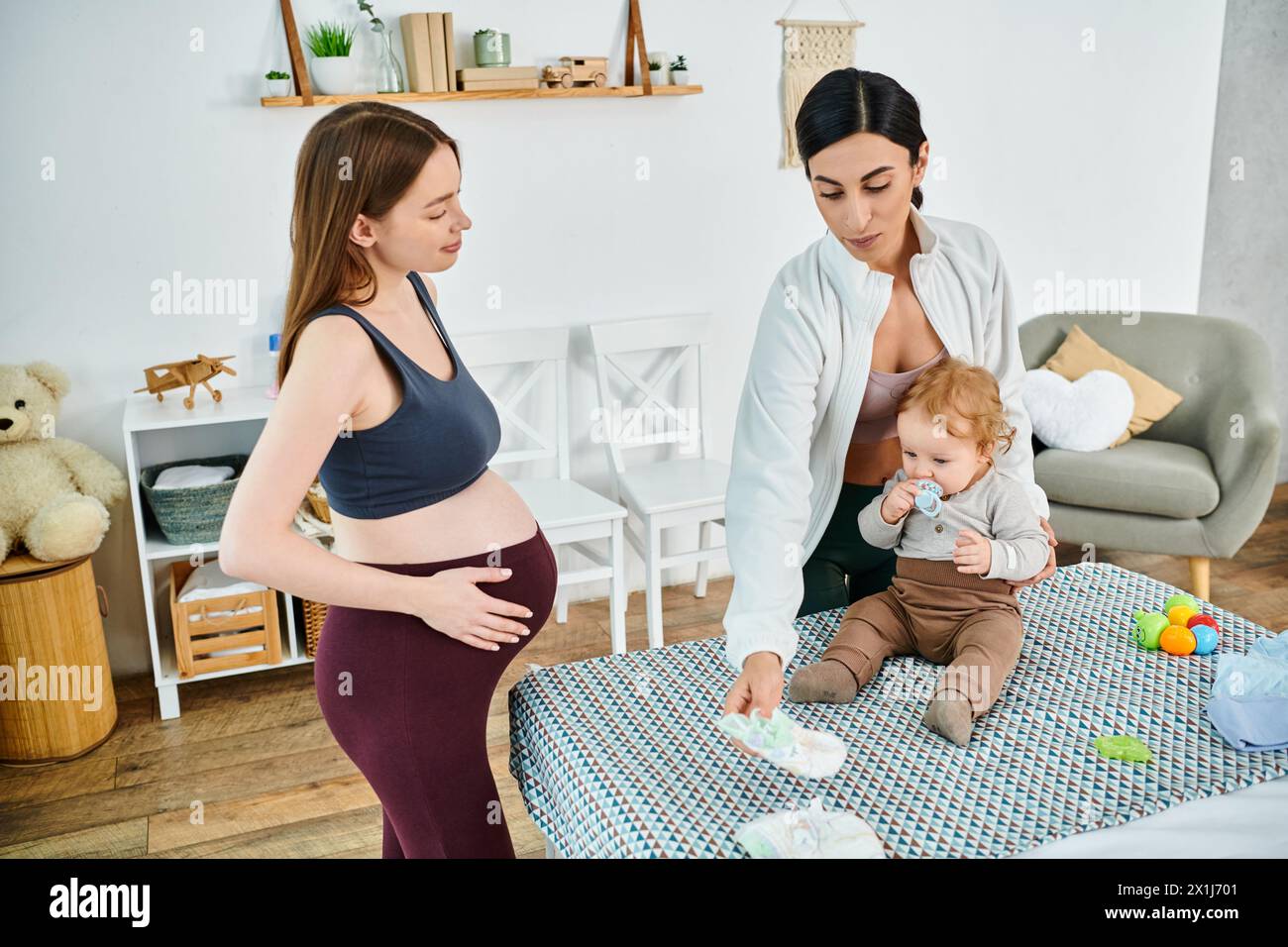 A beautiful young mother stands next to a baby on a bed, receiving ...