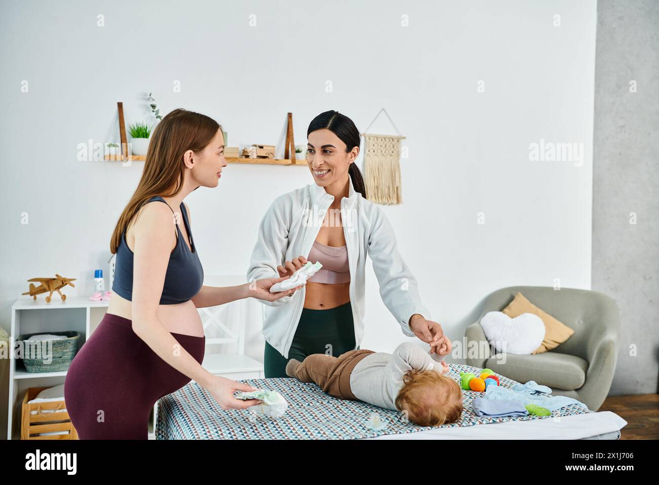 A young beautiful mother lovingly stands next to her baby on a bed ...
