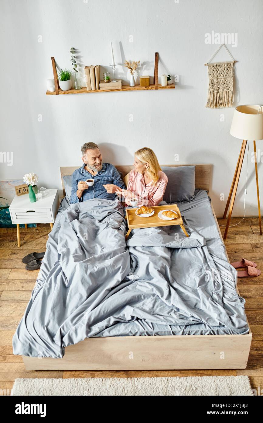 A mature loving couple in cozy homewear, sitting closely together on a ...