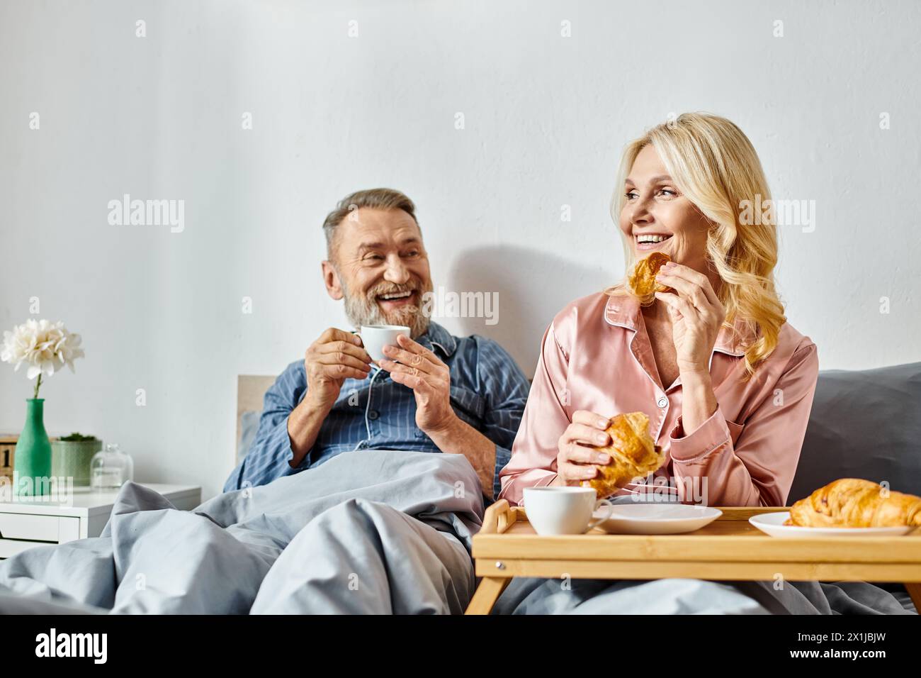Mature couple in homewear sitting on a couch, happily eating food in a ...