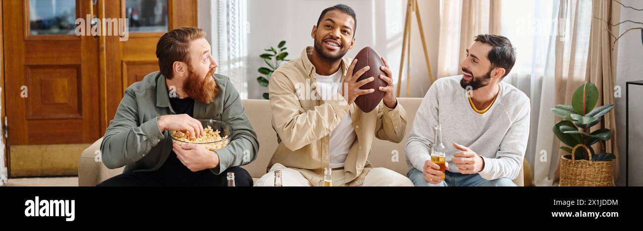 Three diverse men sit on a couch in casual attire, happily holding a ...