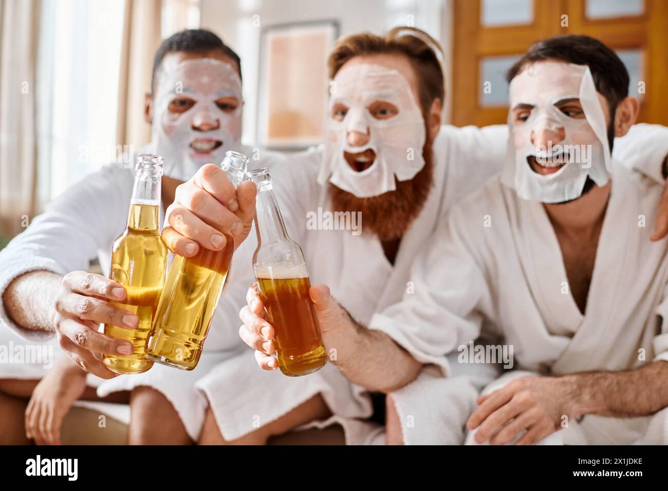 Three diverse, cheerful men in bathrobes, wearing facial masks, enjoy a ...