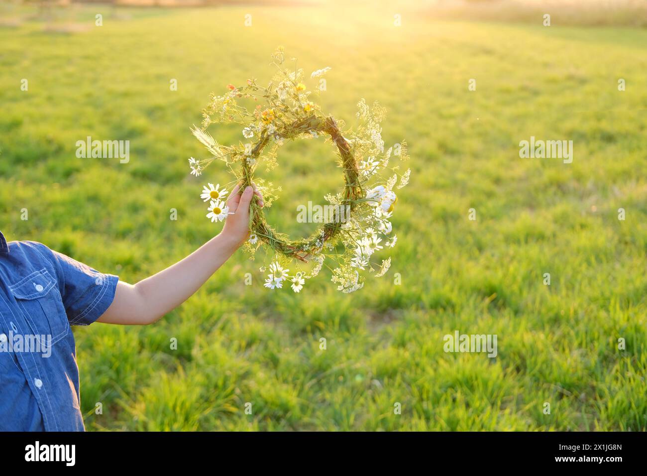 happy boy holding wreath in hand, floral crown on green sunlit meadow ...