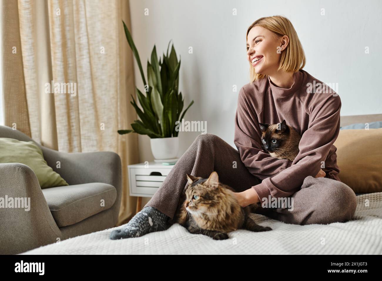 A woman with short hair relaxes on a bed, surrounded by two cuddly cats ...