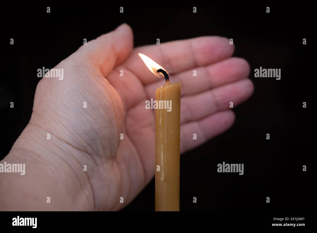 Close-up candle in dark, female hands shield burning flame from wind ...