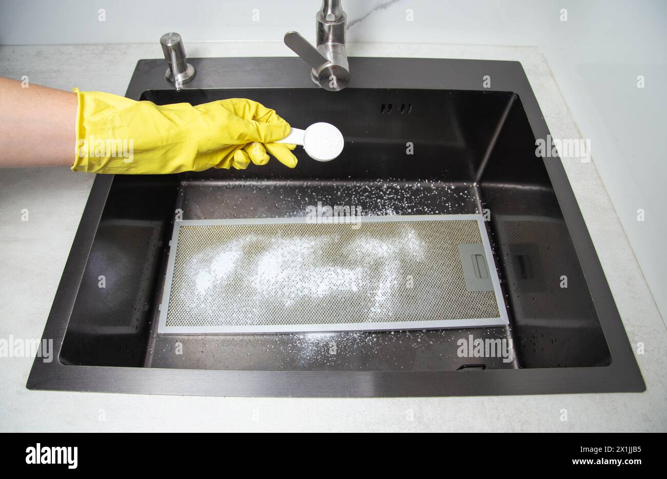 A man's hand in a yellow glove holds a spoon with oxygen bleach against ...