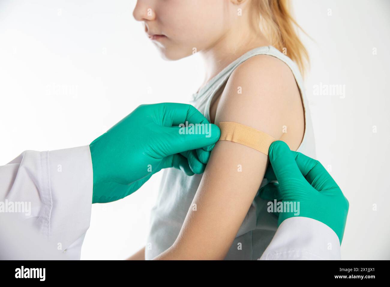 Doctor's hands in green medical gloves stick a plaster on the shoulder ...