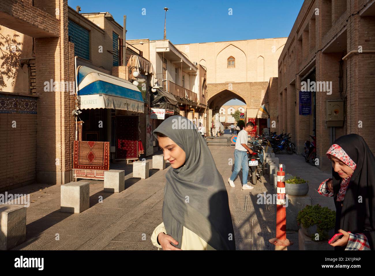 Young Iranian women in hijabs walk in a narrow street in the historical ...