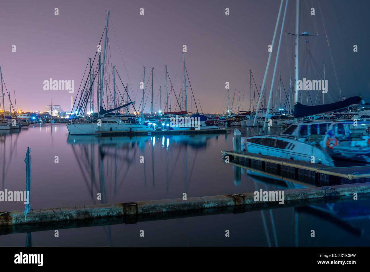 Night view of a boat dock with calm water and many boats and distant ...