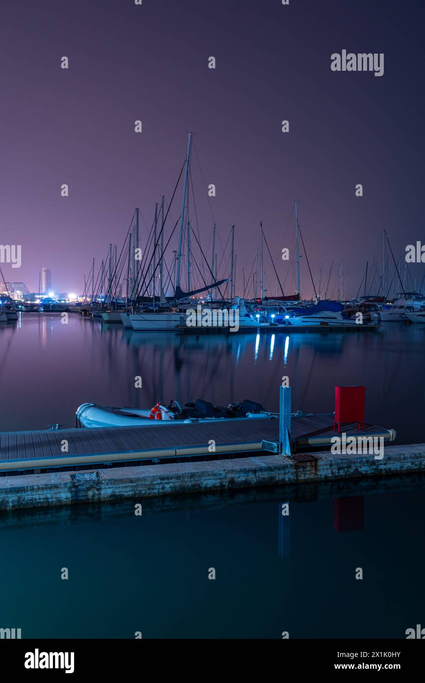 Night view of a boat dock with calm water and many boats and distant ...