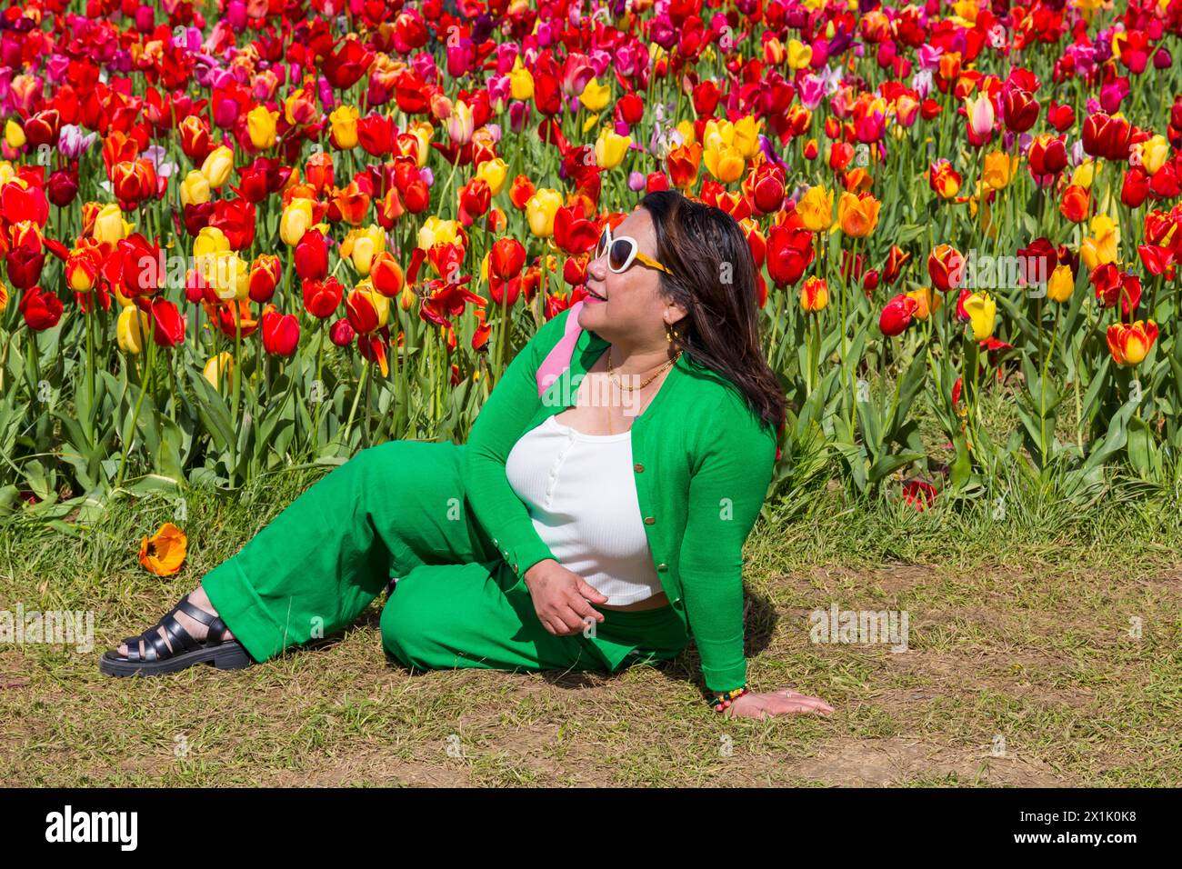 woman wearing green trouser suit and sunglasses sitting by tulips ...