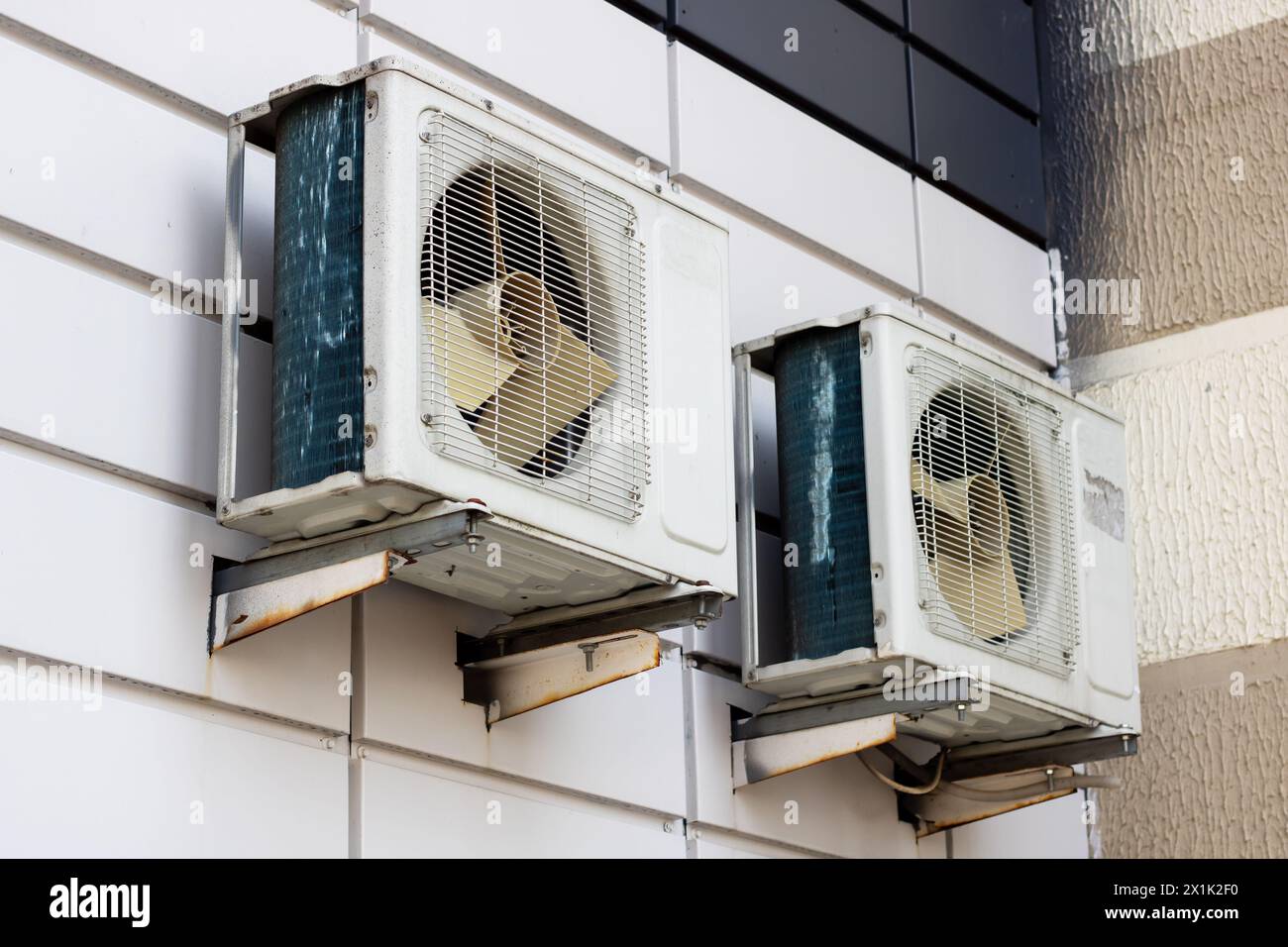 Two air conditioners are fixed on the brick facade of the building, one ...