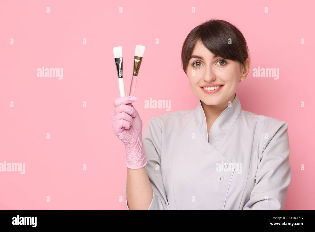 Cosmetologist with cosmetic brushes on pink background Stock Photo - Alamy