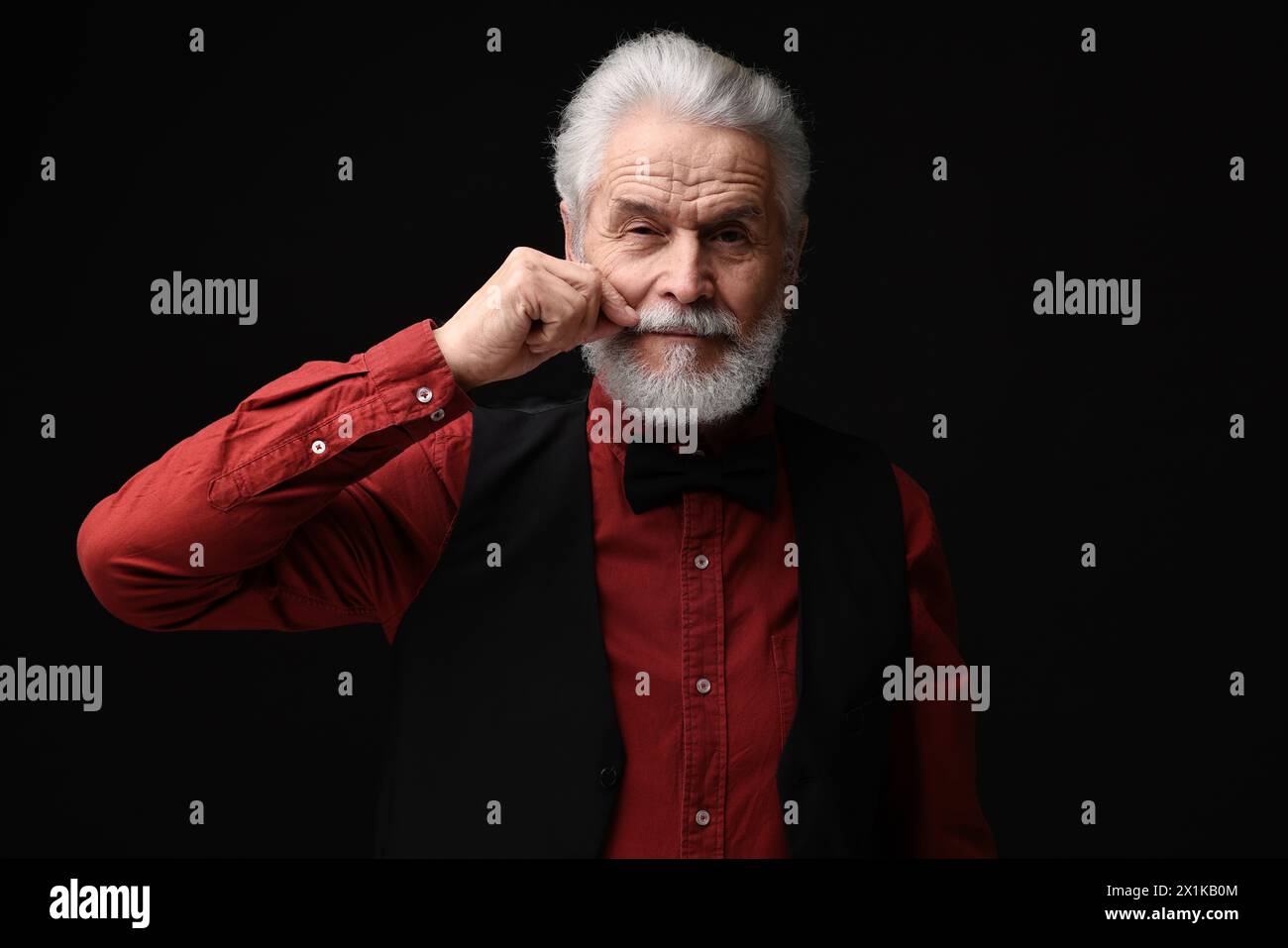 Senior man touching mustache on black background Stock Photo - Alamy