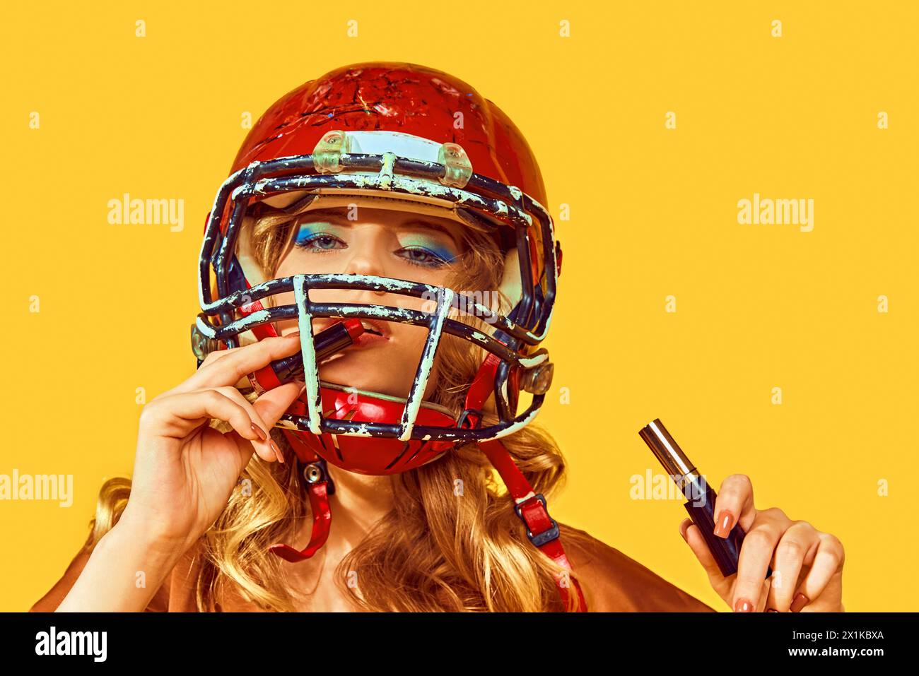 Beautiful woman in elegant attire wearing football helmet makes makeup ...