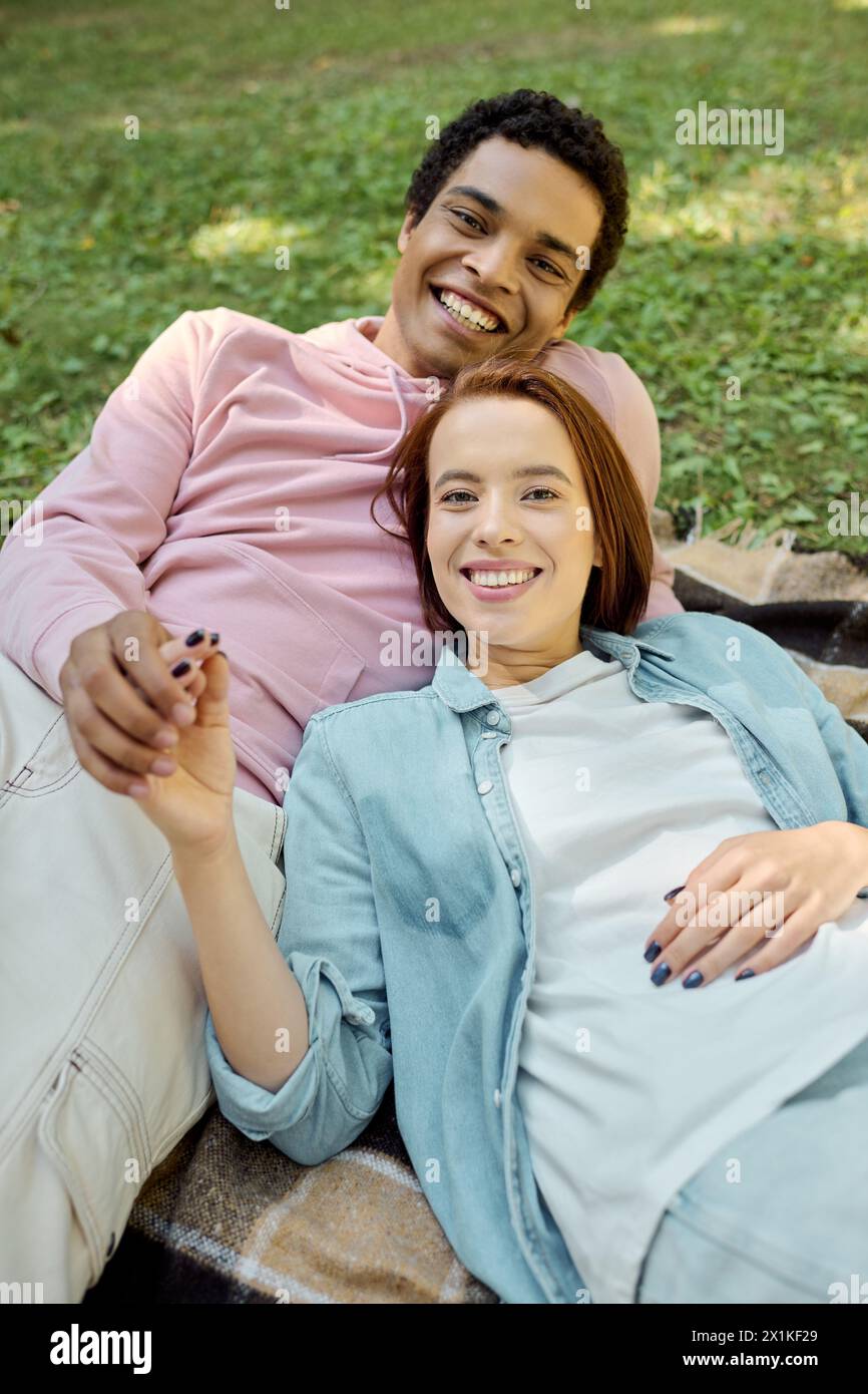 A diverse couple in vibrant attire sit together on a park bench ...