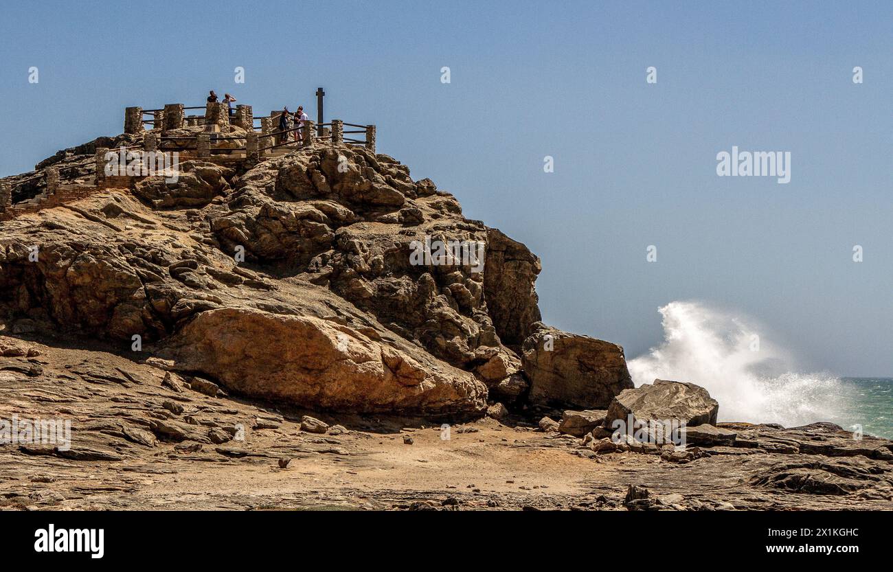 Spray thrown up from the choppy, green sea by the rock mound with a ...