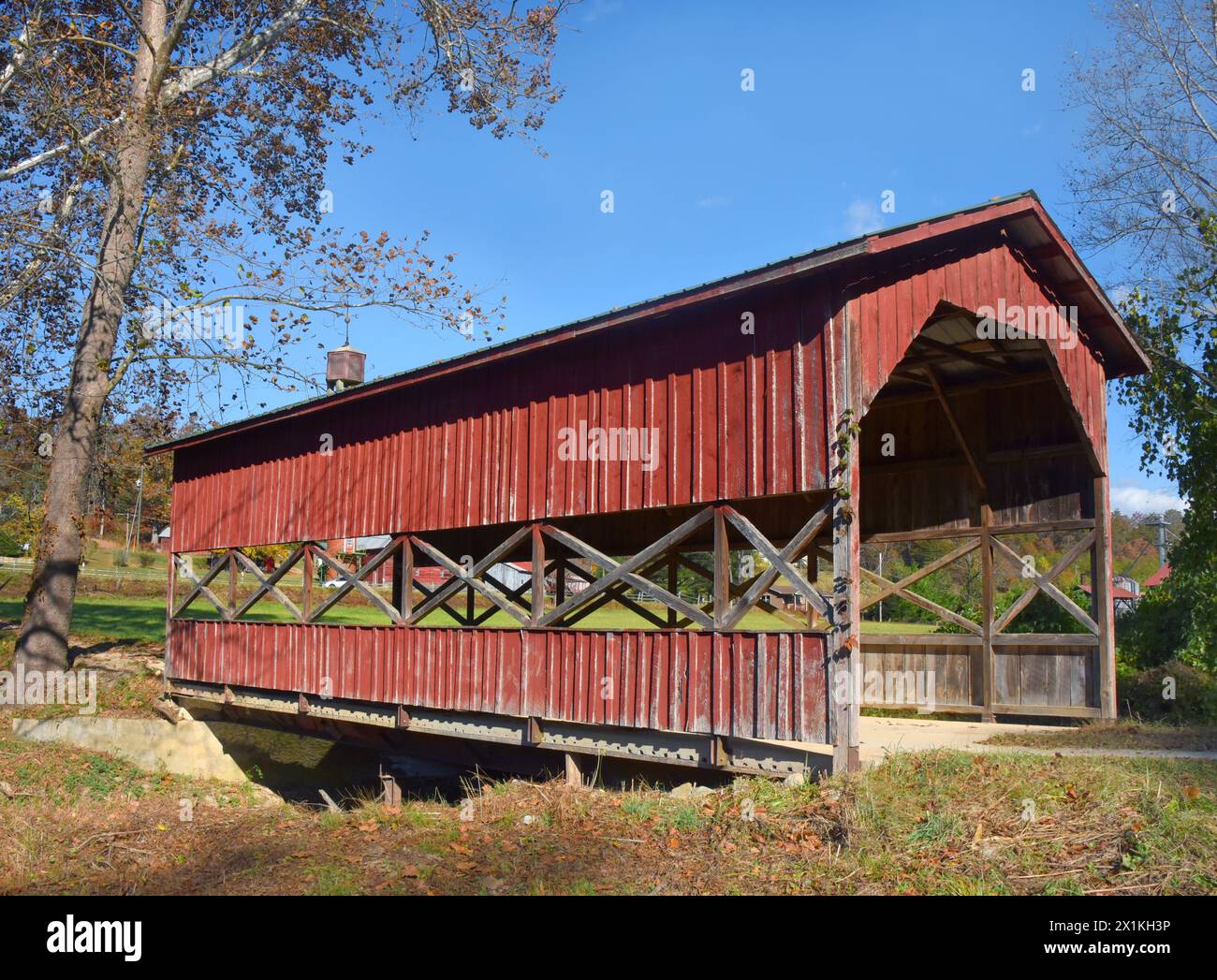 Weathered, wooden covered bridge has faded red exterior. Bridge is ...