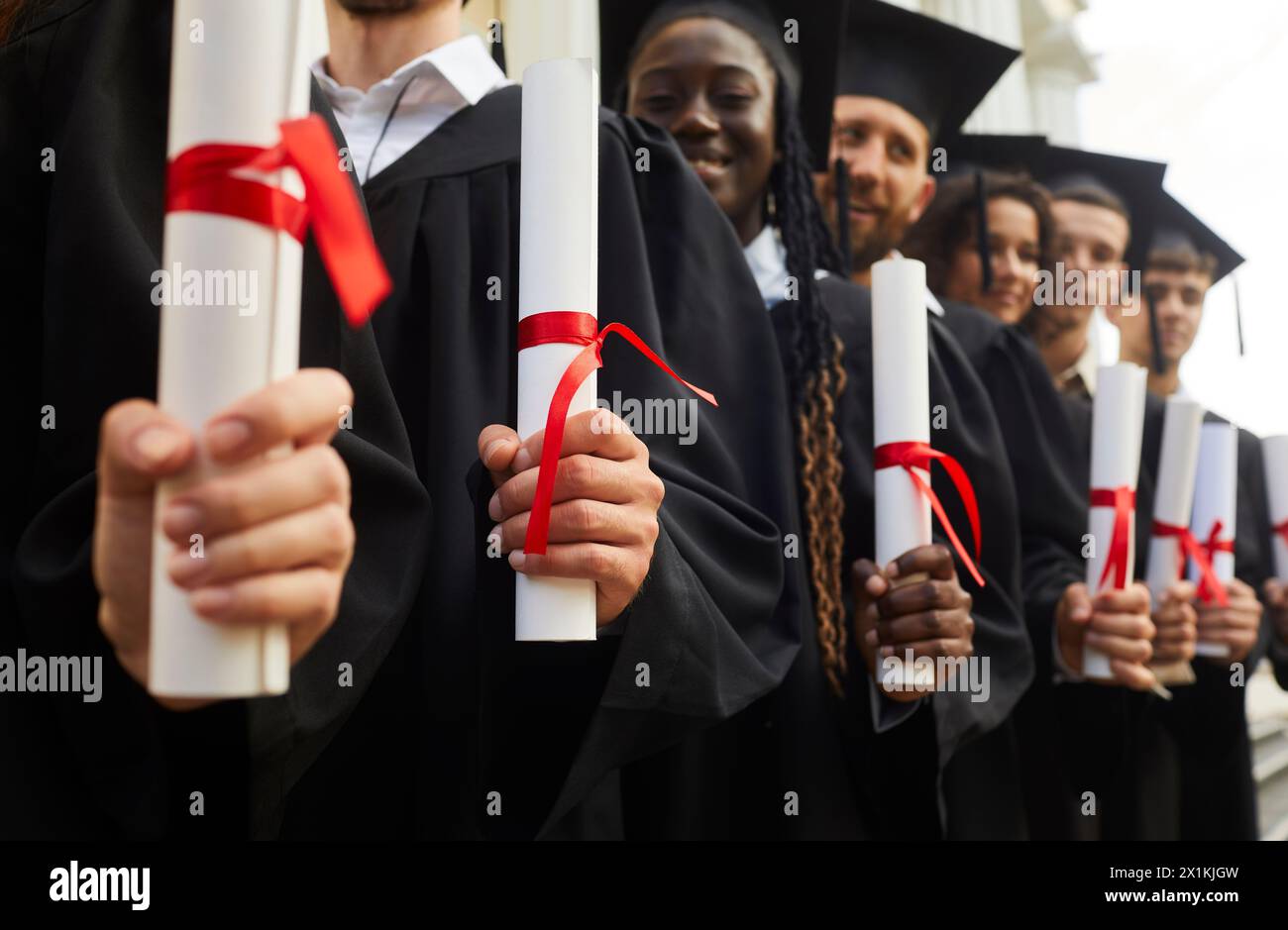 Graduate students standing in a row in black robes with diplomas in ...