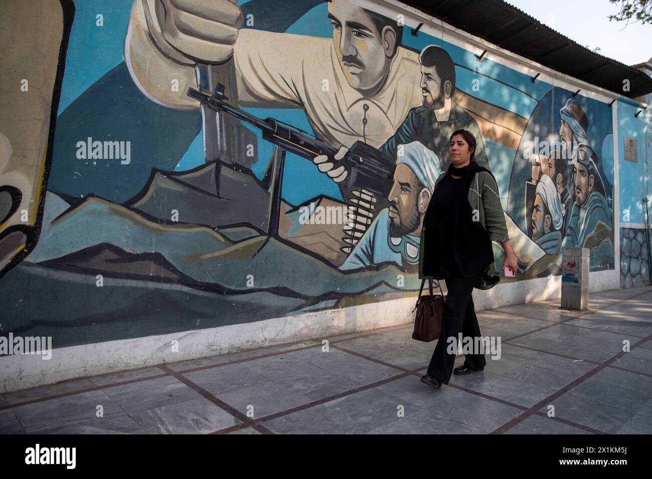 Tehran, Iran. 14th Apr, 2024. A woman walks past a mural in Felestin ...