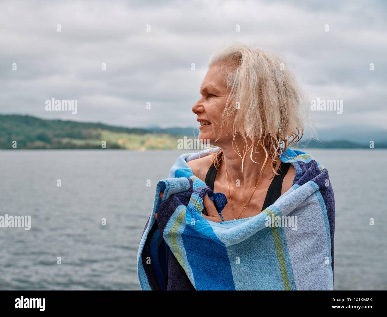 A senior open water wild swimmer warms themselves up with a towel after ...