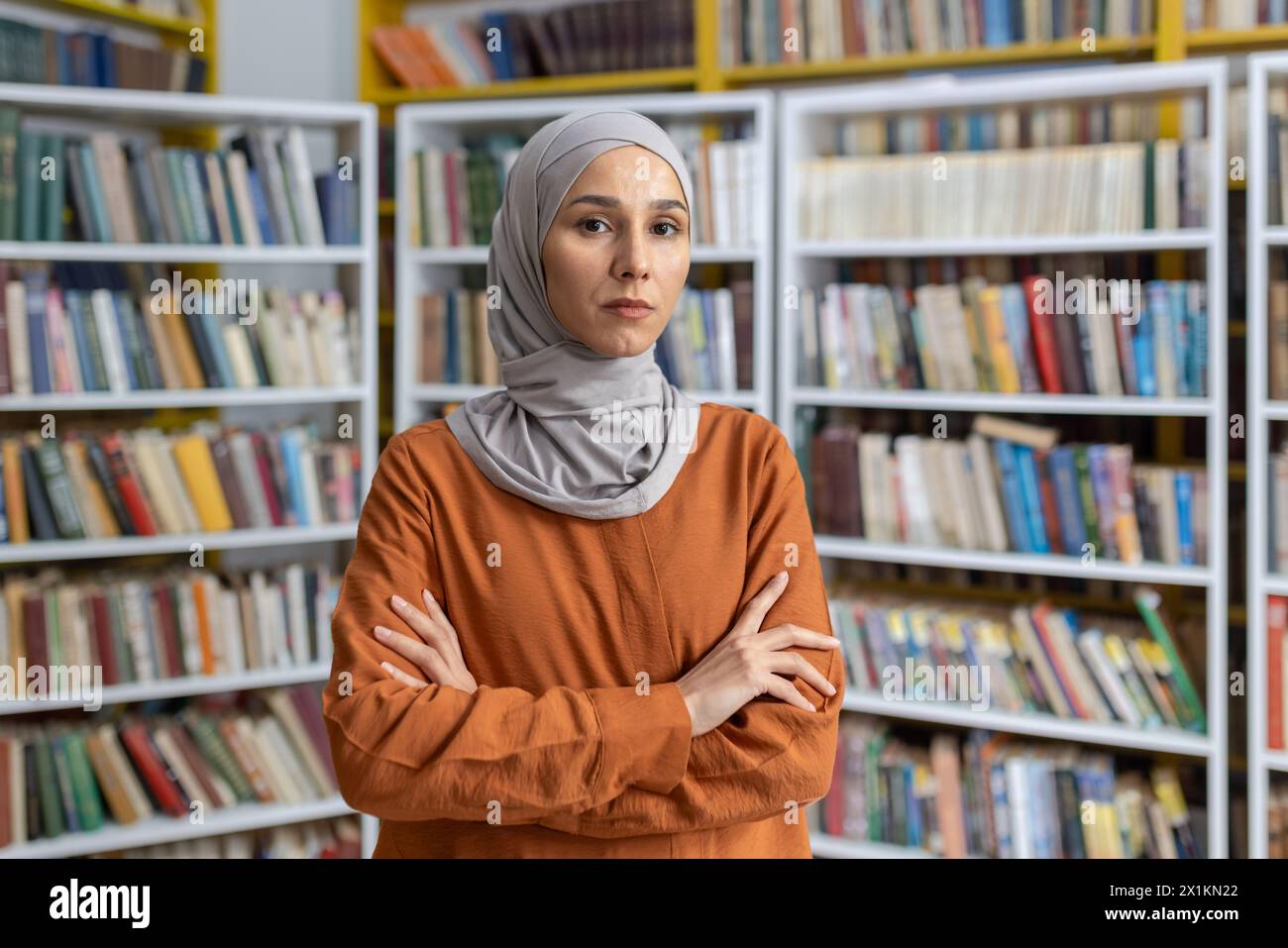 A confident Muslim woman in a hijab stands with her arms crossed in a ...