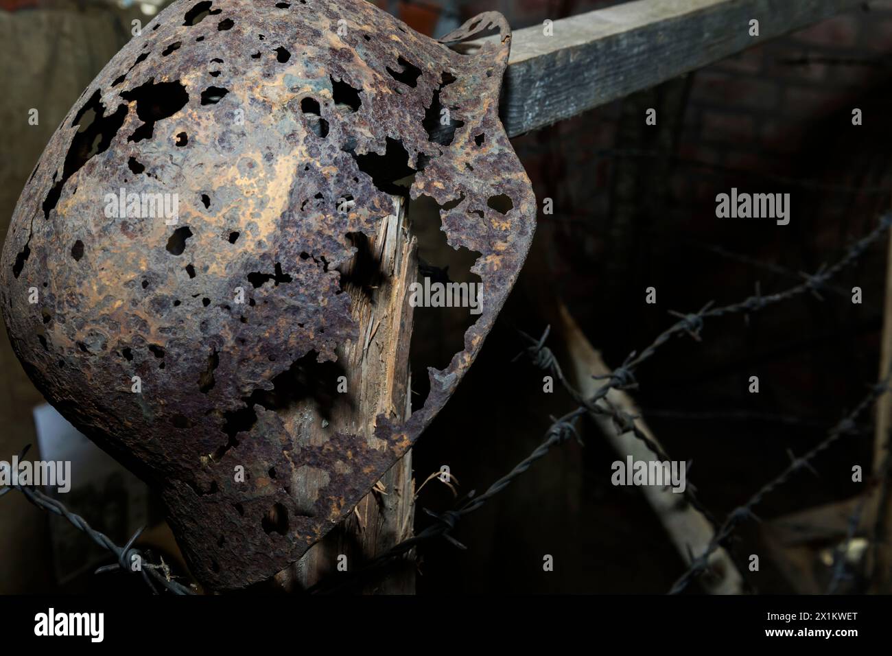 An artifact, a rusty helmet, rests on a barbed wire fence entangled ...