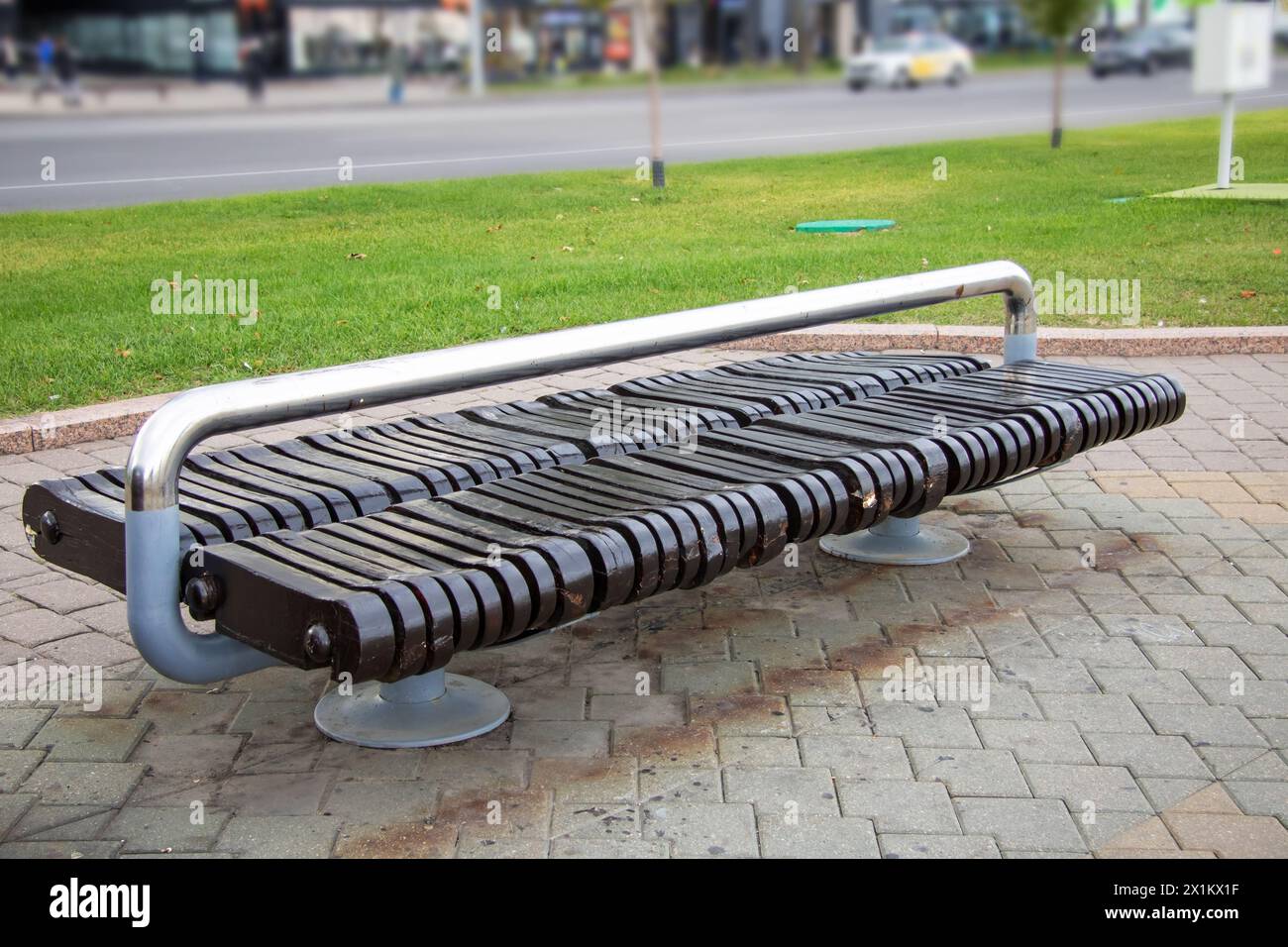 An outdoor bench with a metal railing is placed on a brick sidewalk ...
