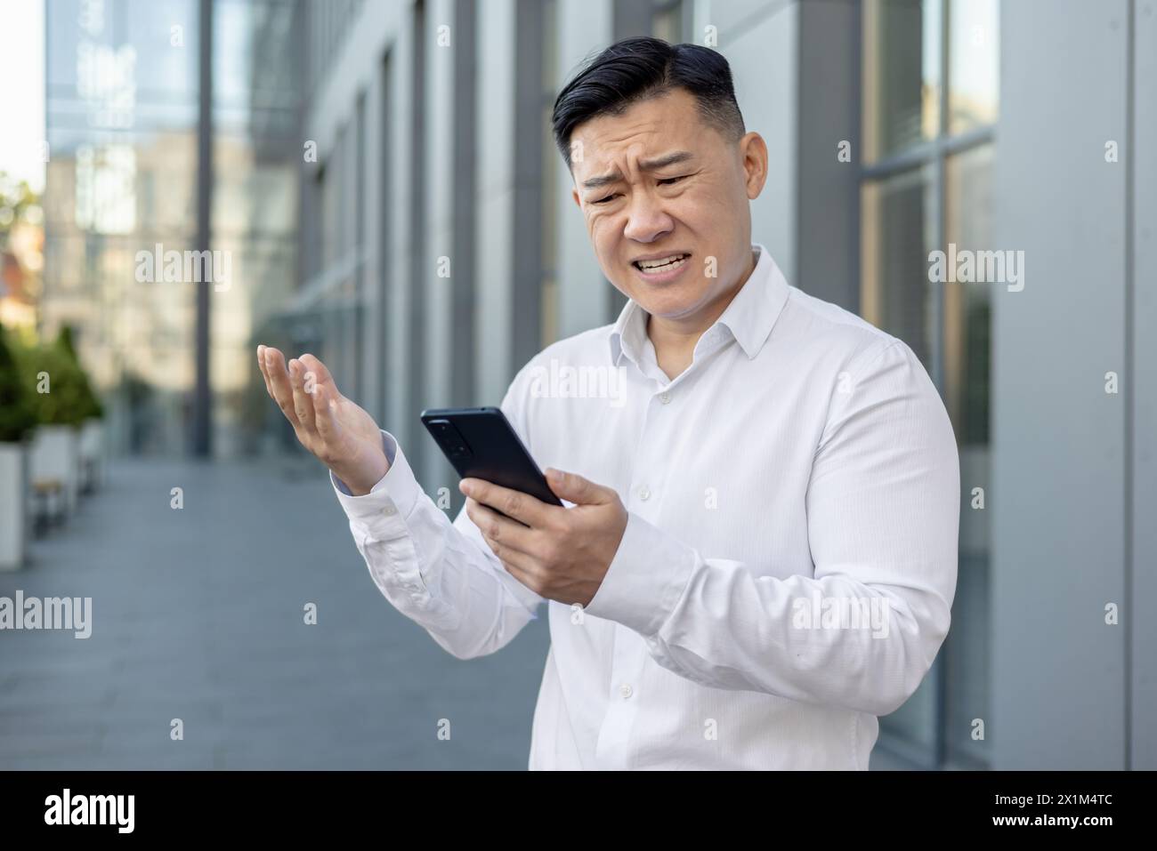 Angry and worried young Asian male businessman standing outside a ...