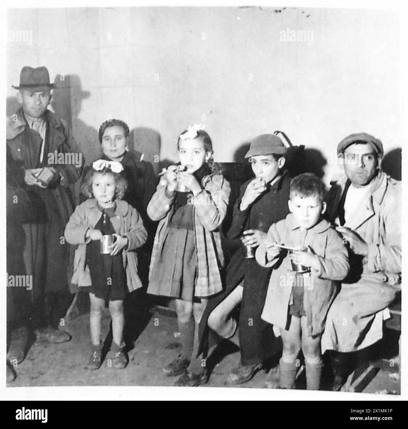 Children eat American 'C' rations in a church corner while refugees are ...