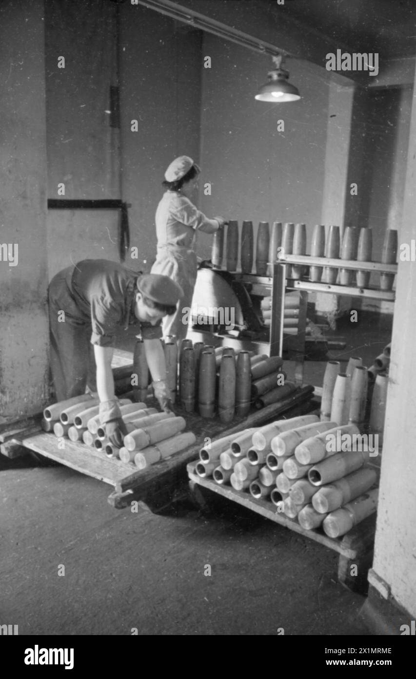Two female munitions workers load shells onto a conveyor belt at a ...