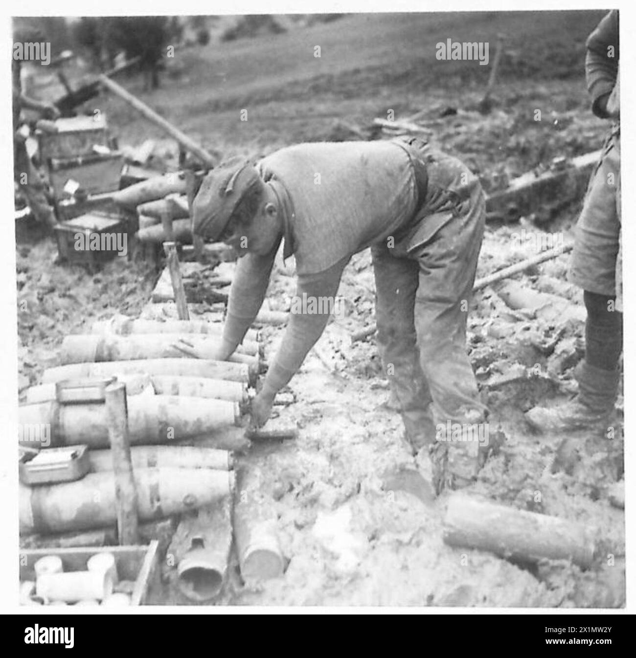 A gunner works ankle-deep in mud while setting fuses during British ...