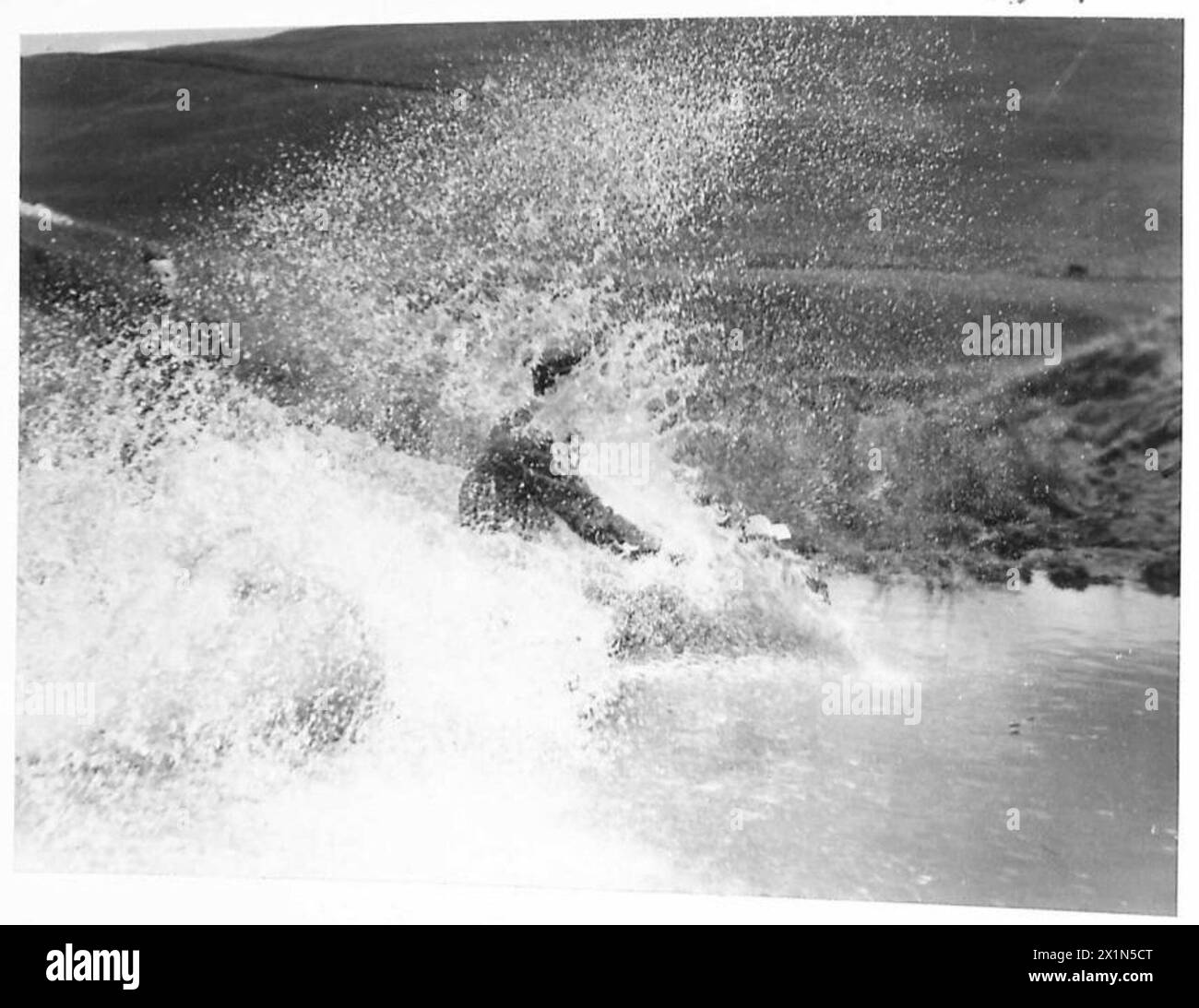 A British Army competitor navigates a water obstacle, creating a splash ...